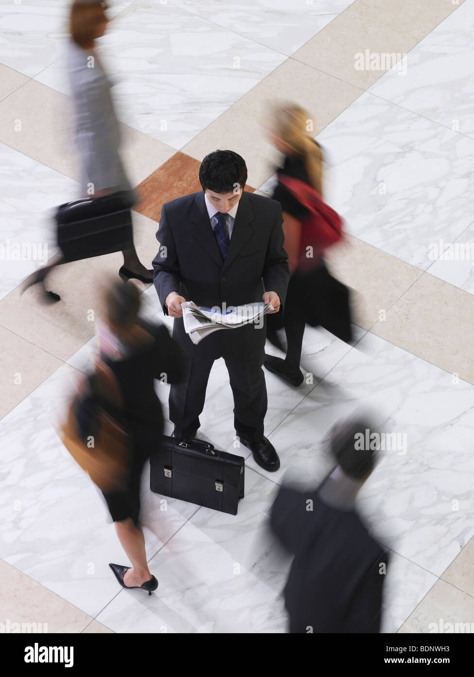Business man reading newspaper amongst people walking, elevated view ...