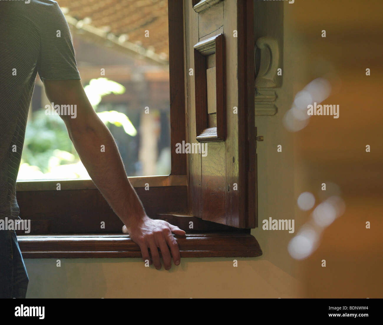 Young man looking trough window, leaning on windowsill, back view ...