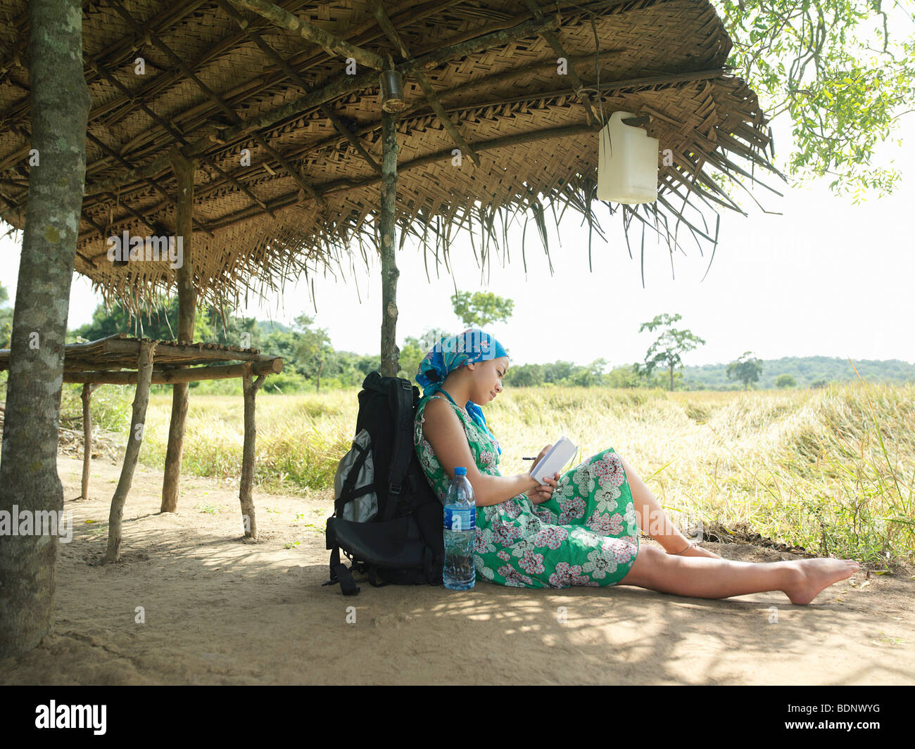 Young woman wearing dress sitting in shade of hut roof Stock Photo - Alamy