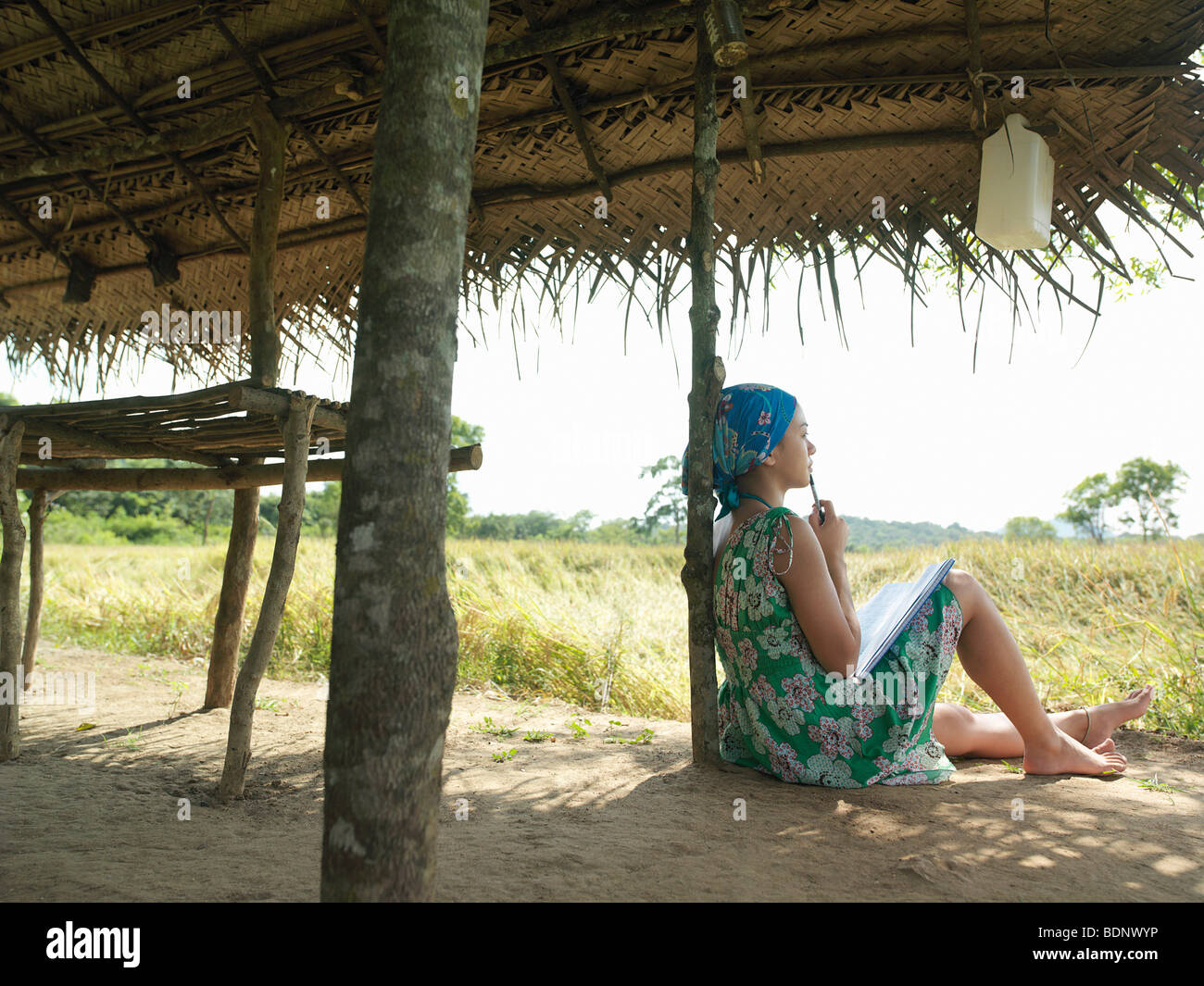 Young woman wearing dress sitting in shade of hut Stock Photo - Alamy