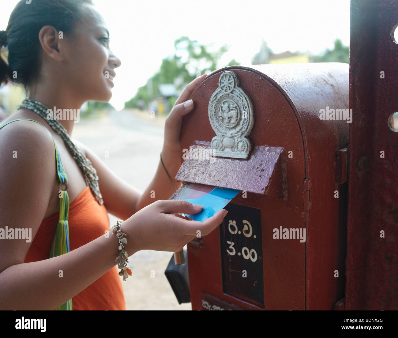 Young woman putting postcard to mailbox, smiling Stock Photo - Alamy