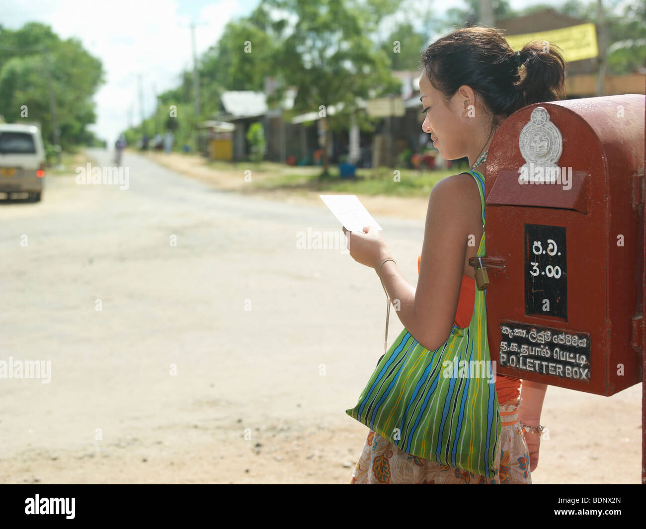 Young woman standing by mailbox reading postcard Stock Photo - Alamy