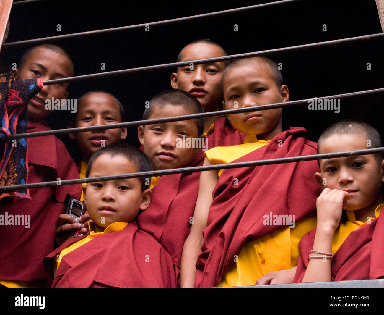 A group of novice Buddhist boy monks look out from a barred window in ...
