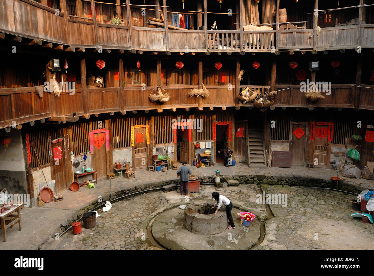 Chinese woman drawing water from the well in the courtyard of a wooden ...