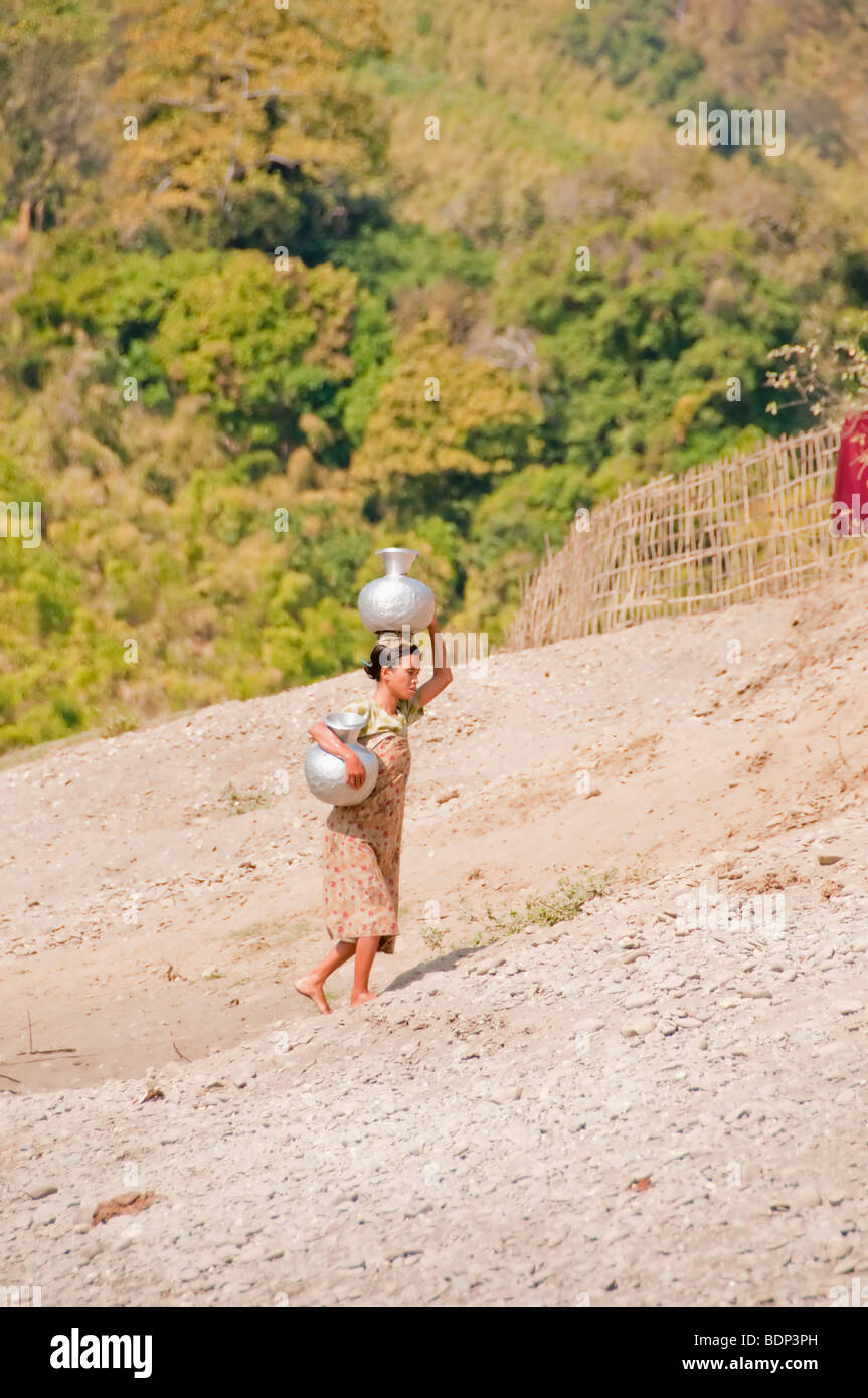 Chin woman carrying traditional water jars made from beaten metal up to ...