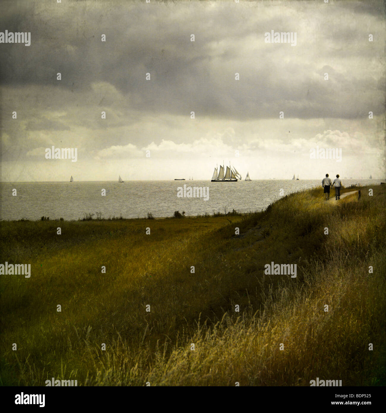 man and woman walking along a path by the sea with tall ships Stock ...