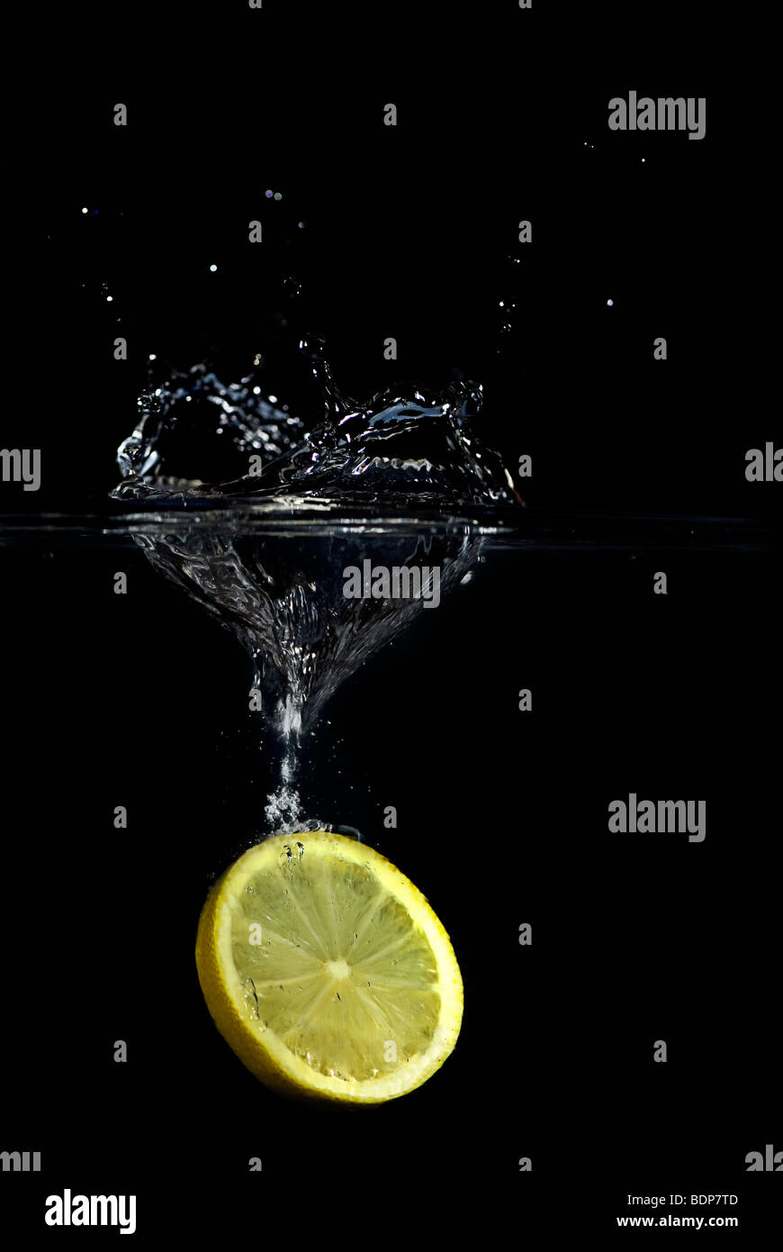 A lemon dropped into water creating a splash and bubbles. Isolated on black Stock Photo - Alamy