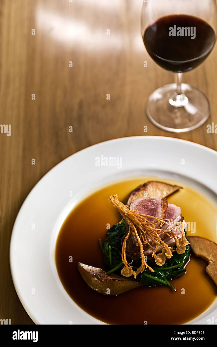 Crispy duck on a bed of spinach served with red wine in a restaurant ...