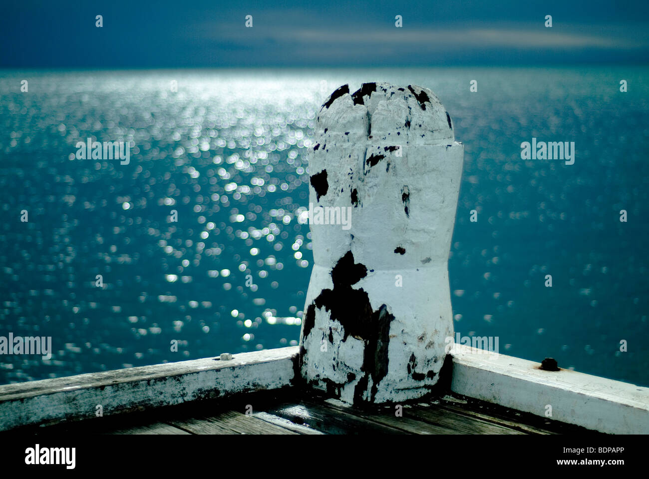 A wooden post pianted white with sparkling blue sea in the distance ...