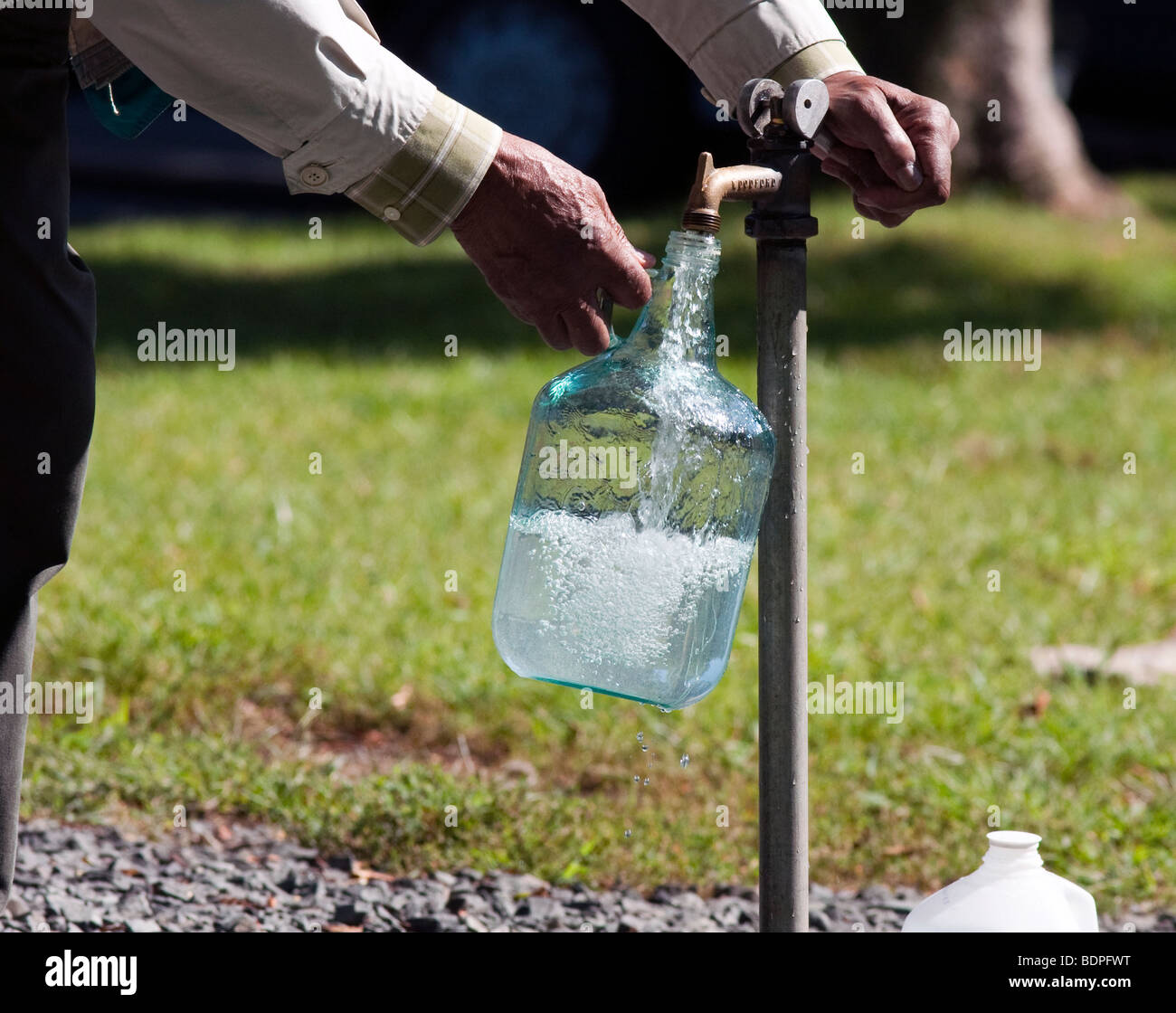 Filling a large glass jug at an outdoor tap with pure clean well water ...