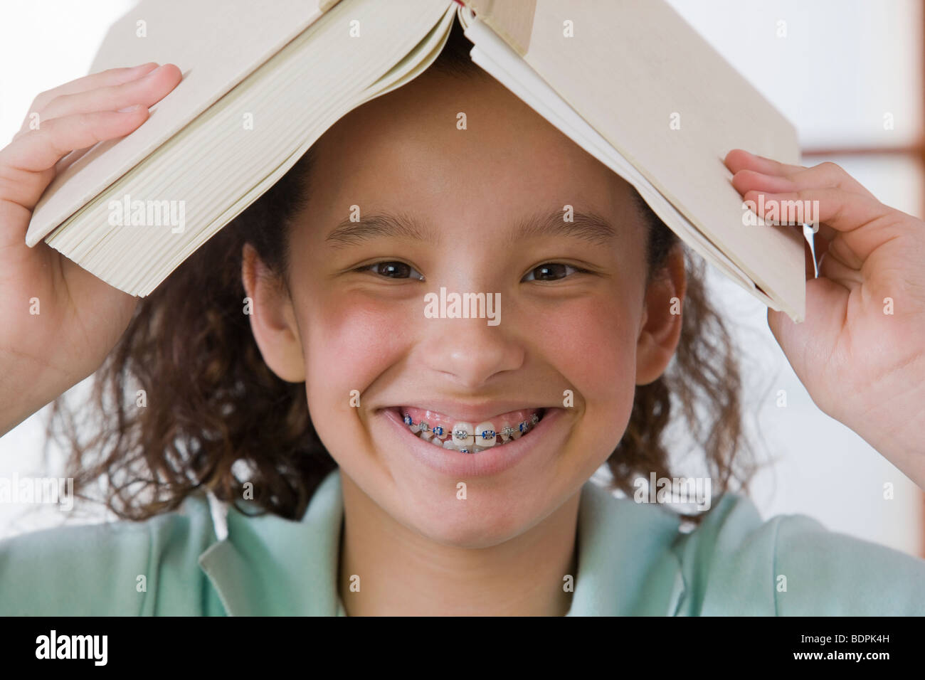 Portrait of a girl putting book on her head and smiling Stock Photo - Alamy