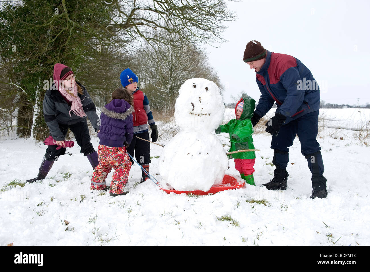A father and four children try to pull a snowman on a sledge Stock ...