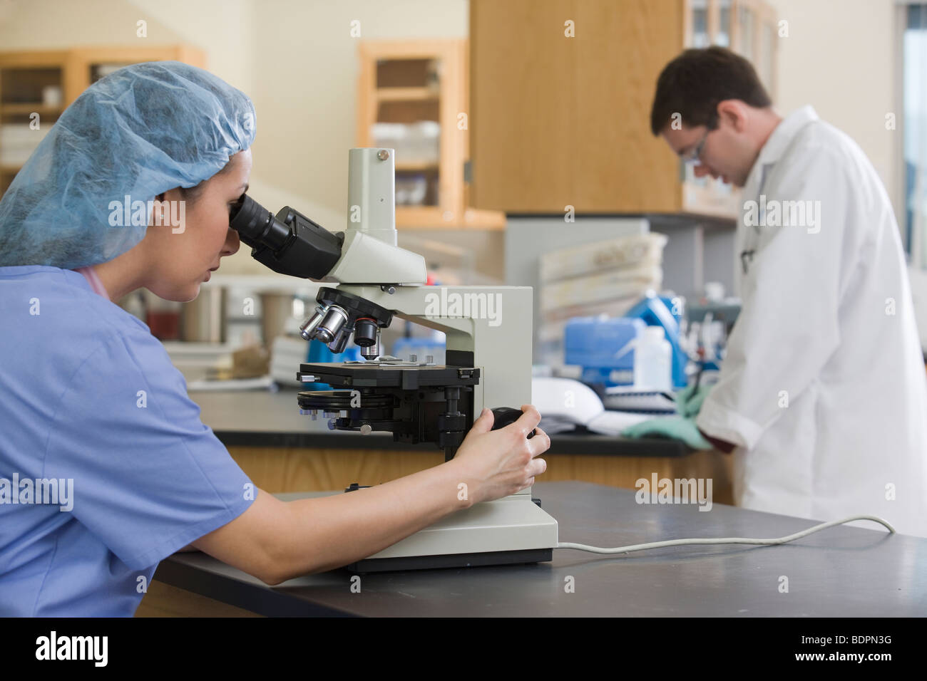 Female lab technician analyzing a sample through a microscope Stock ...