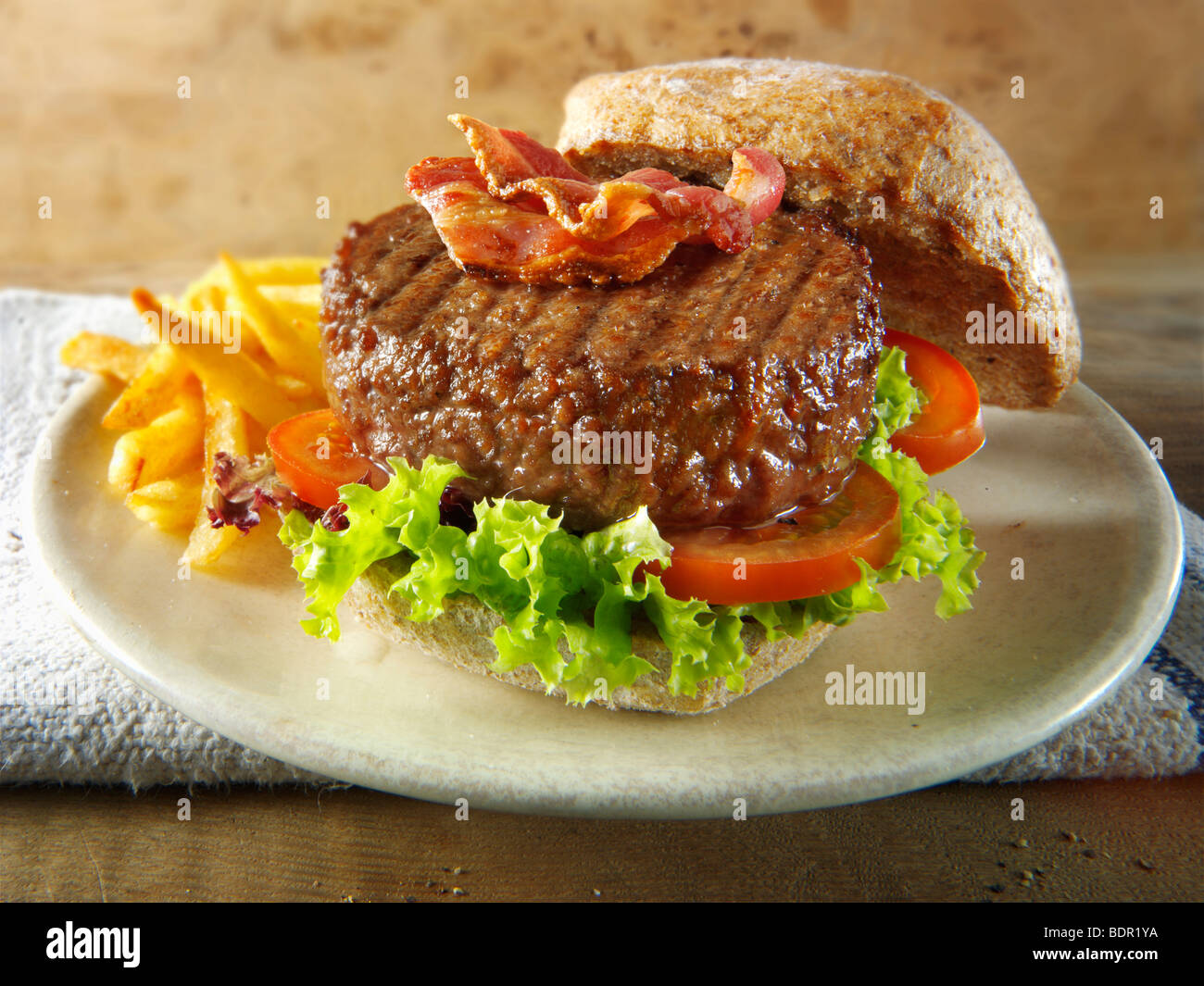 Beef burger with bacon in a wholemeal bun with salad and french fries ...