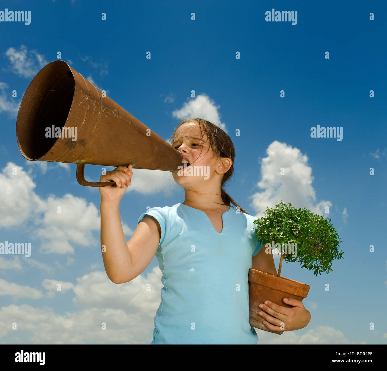 young girl holding a small tree and shouting with a megaphone against ...