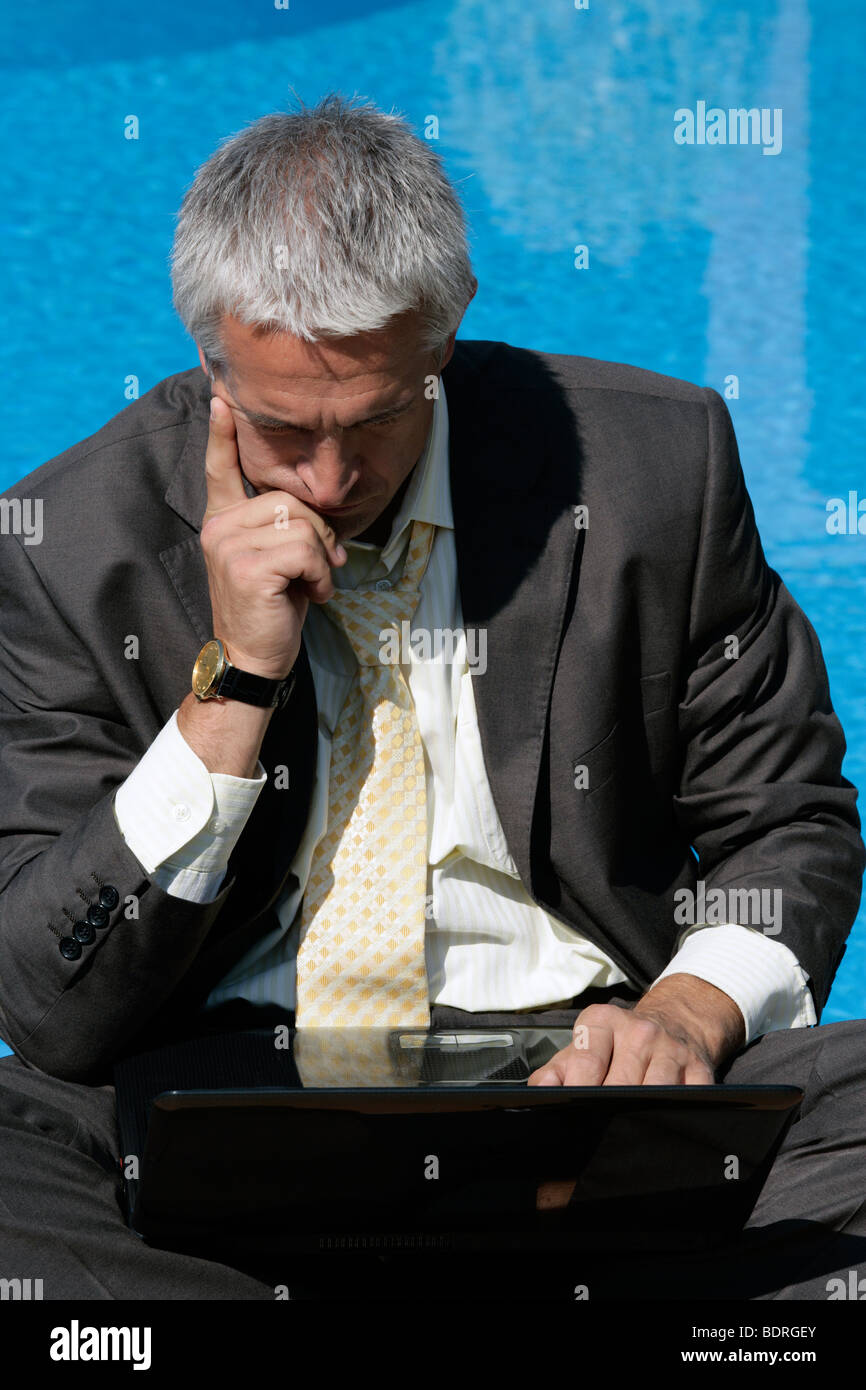 Worry businessman with laptop computer sitting next to swimming pool ...