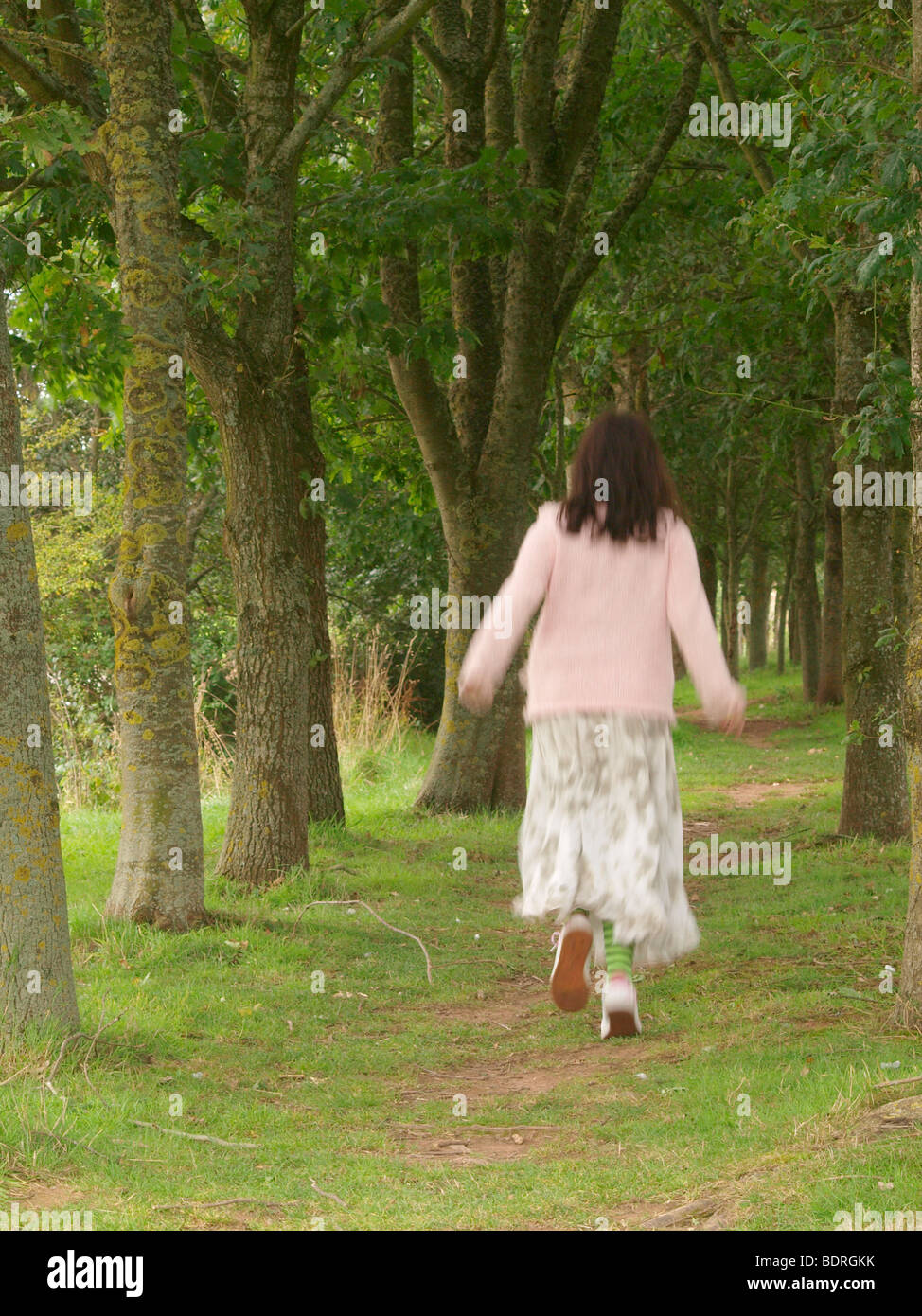 Young girl skipping along a path through the trees Stock Photo - Alamy