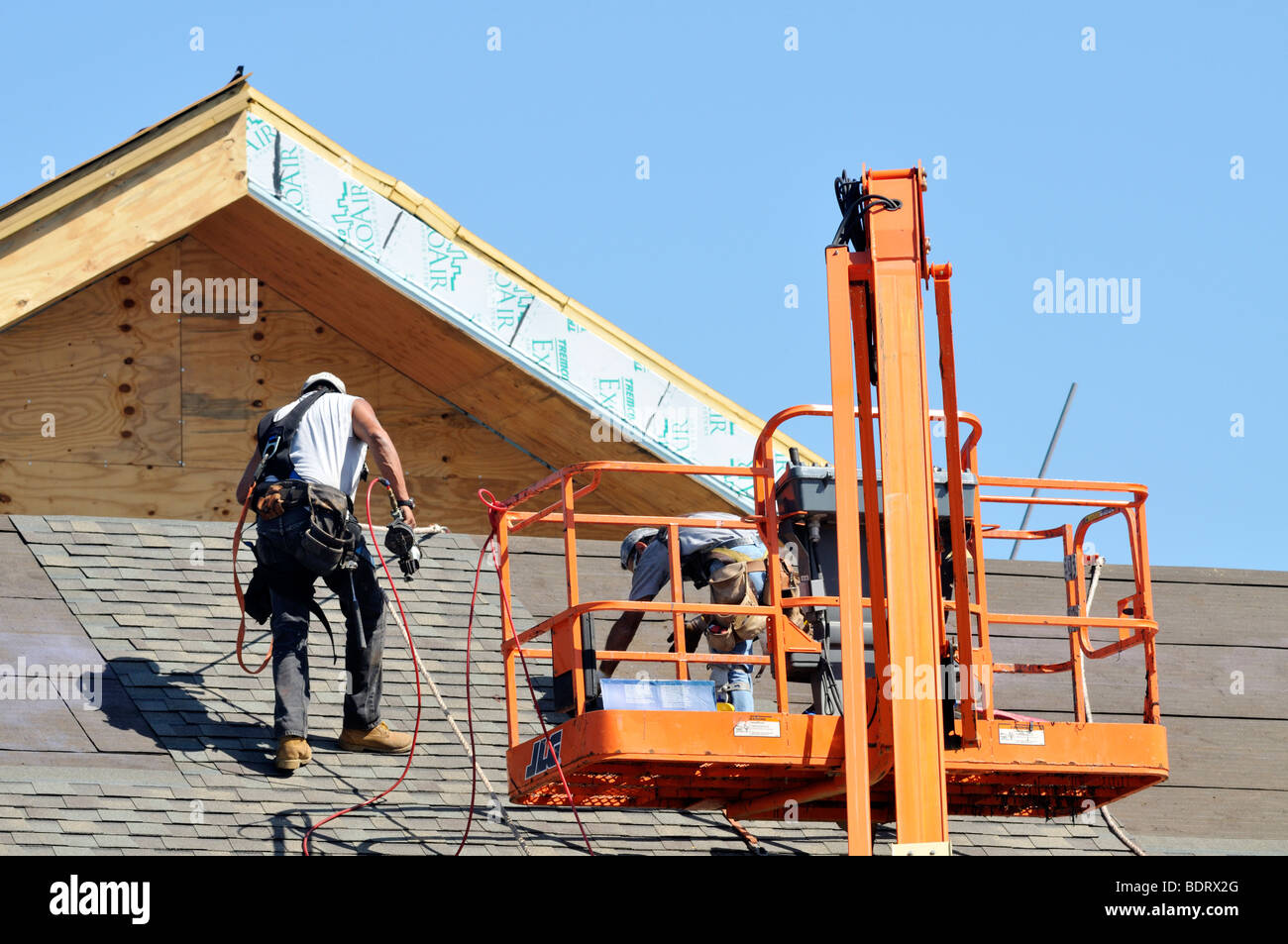 Construction workers laying shingles on roof exterior of new building ...