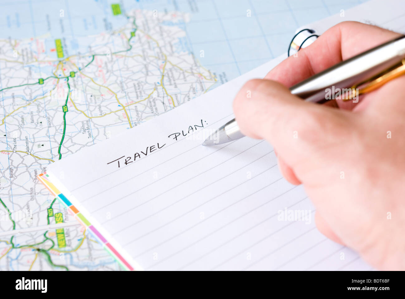 Hand writing travel plan in a lined spiral notepad arranged on a map ...