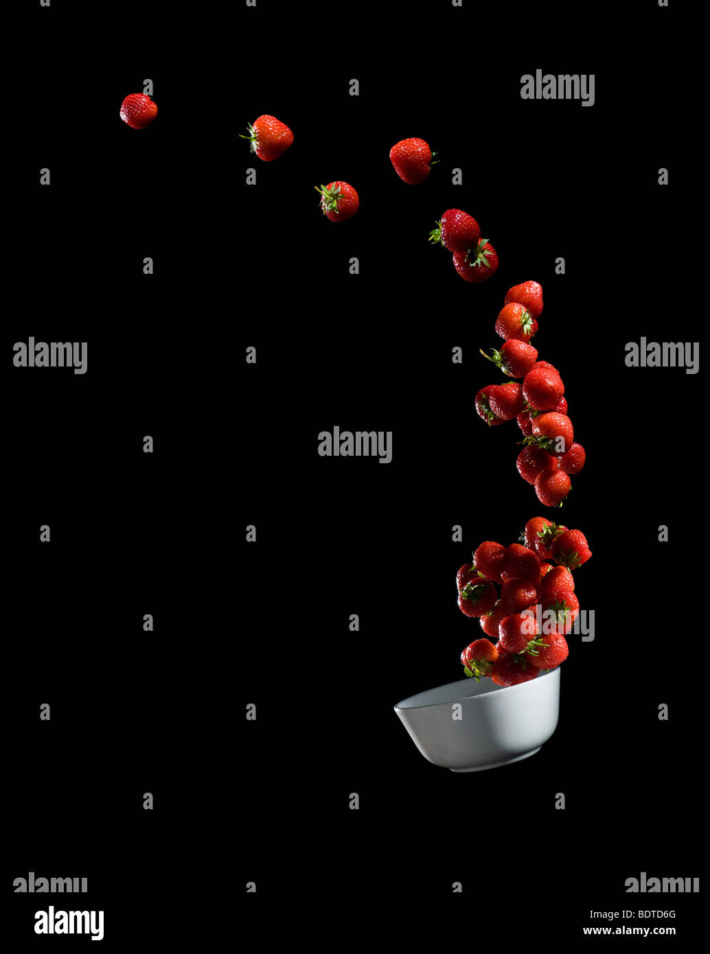 A bowl of strawberries dropping on a black background Stock Photo - Alamy