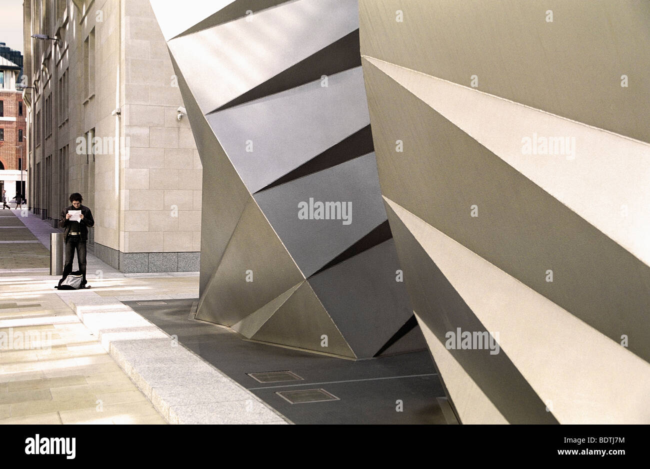 City of London street - Young man reading by a contemporary sculpture ...