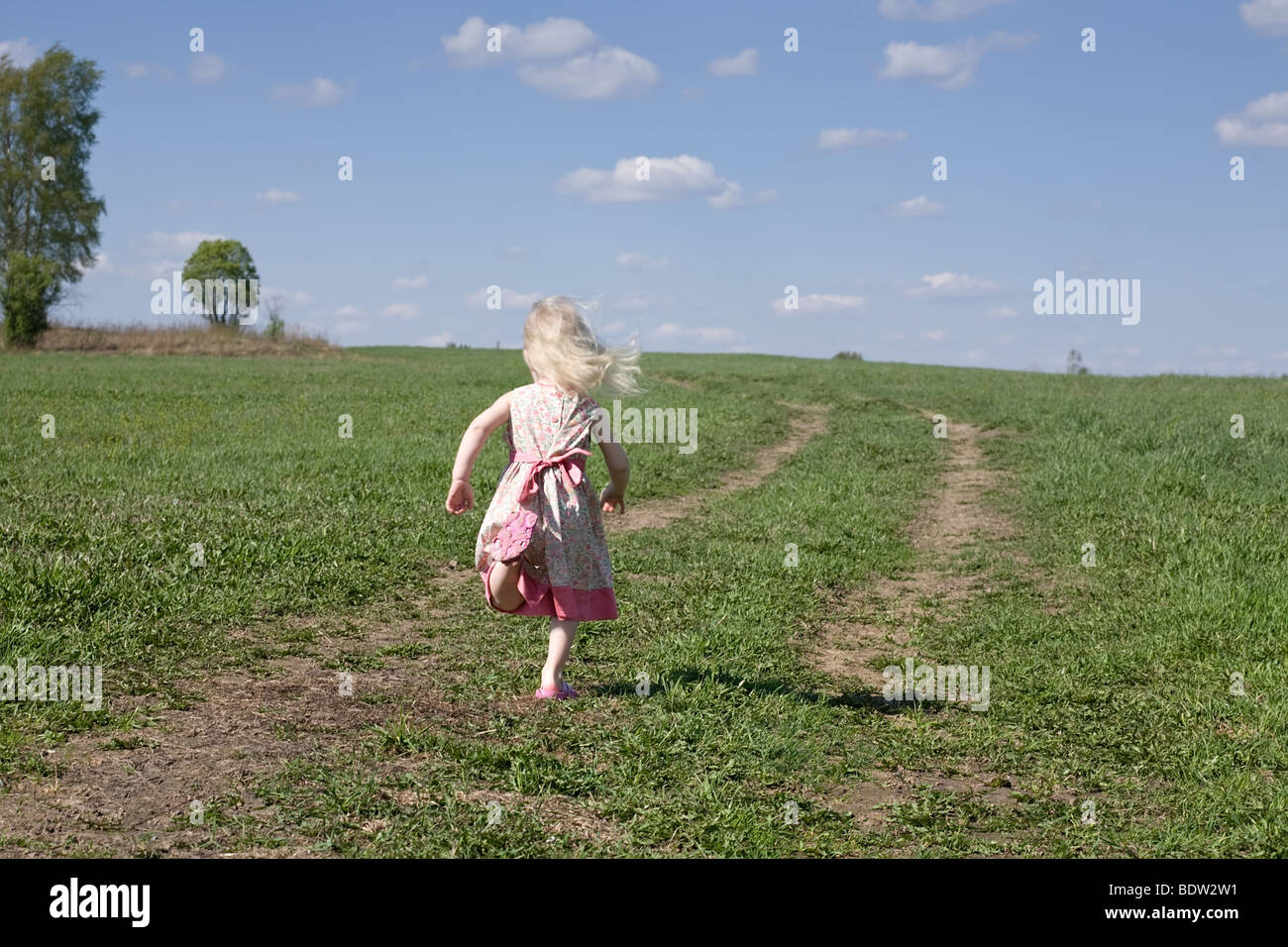 little girl running along the road across green summer meadow Stock ...