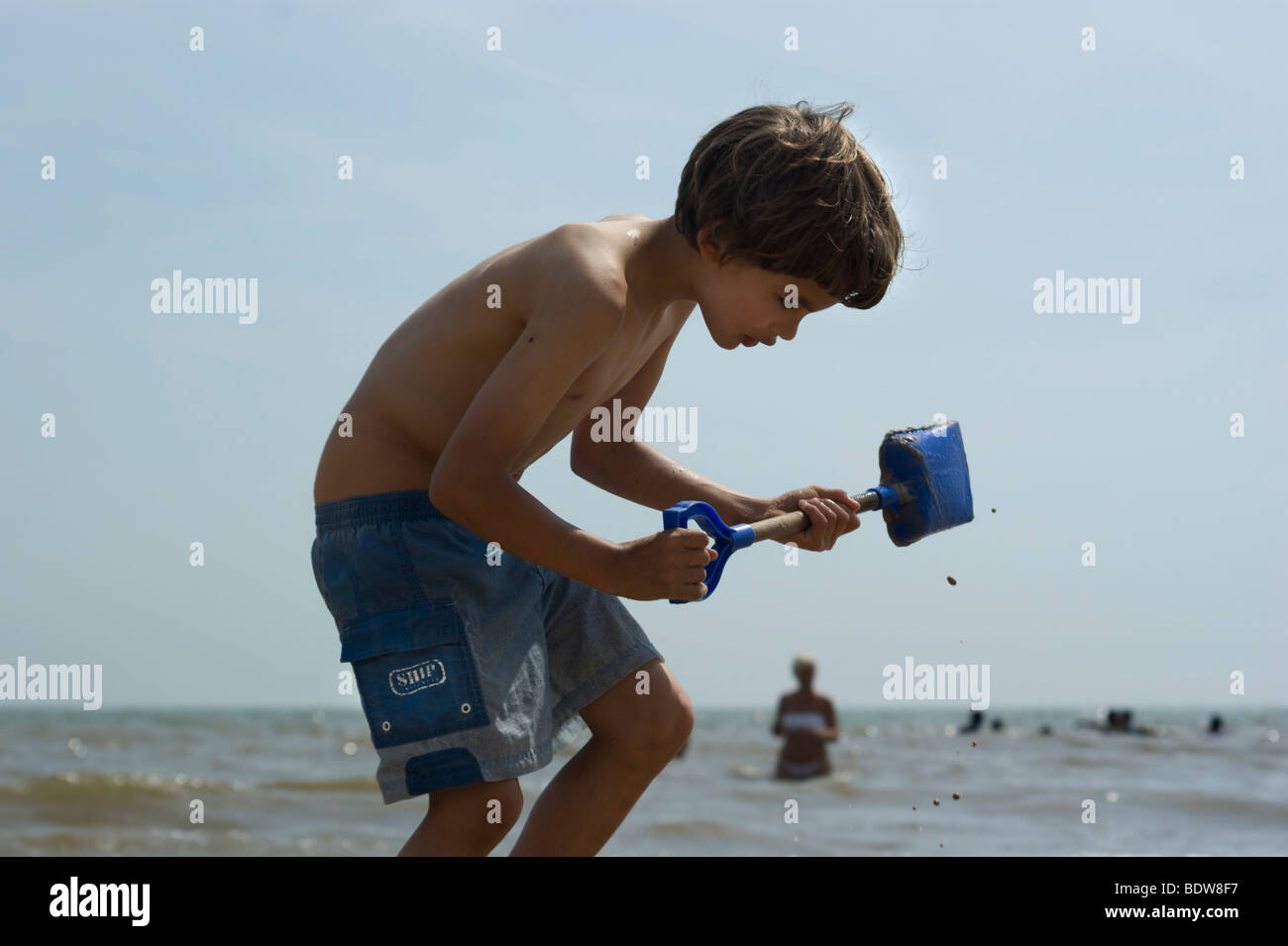 Young boy (8 yr old) shovels at the beginnings of his sandcastle on the ...