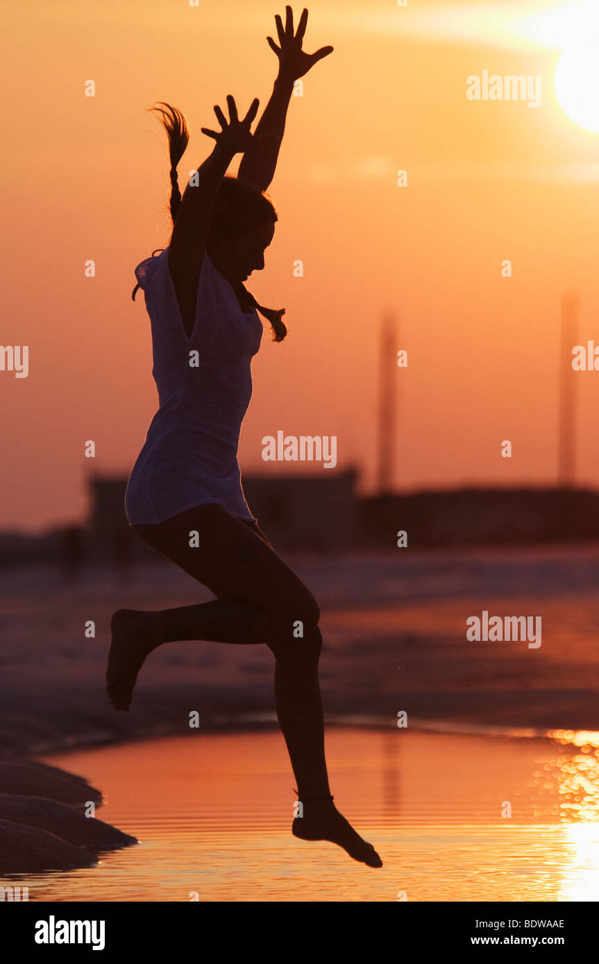 Young oman jumping across pool of water on white sand beach late ...