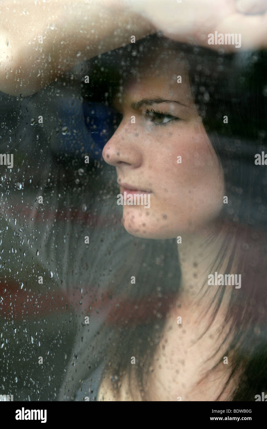 Dark haired woman looking out a rain soaked window Stock Photo - Alamy