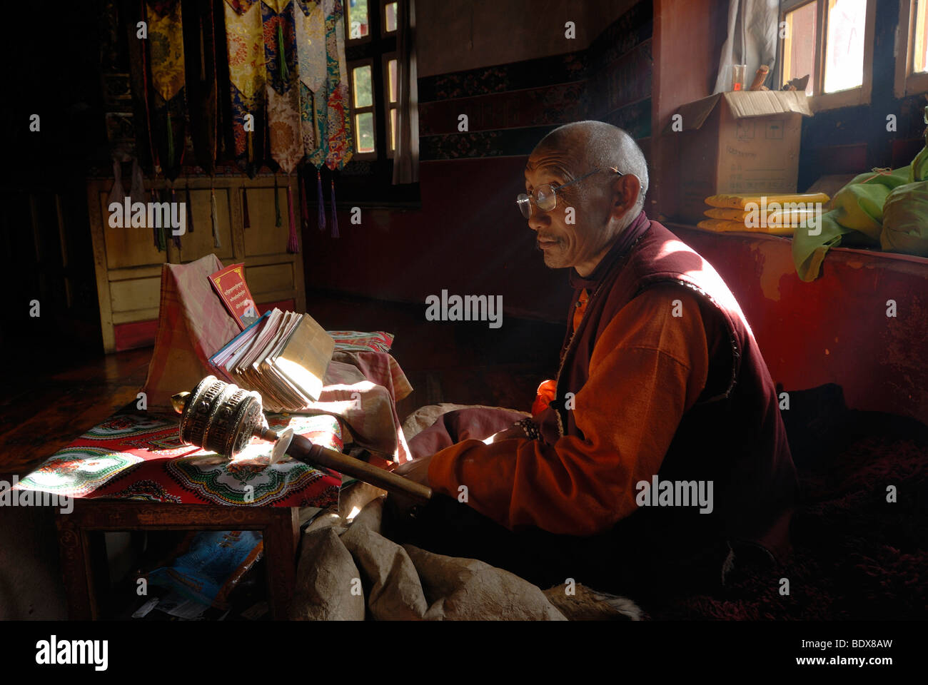 Monk sitting and reciting Tibetan texts with prayer wheel in front of a ...