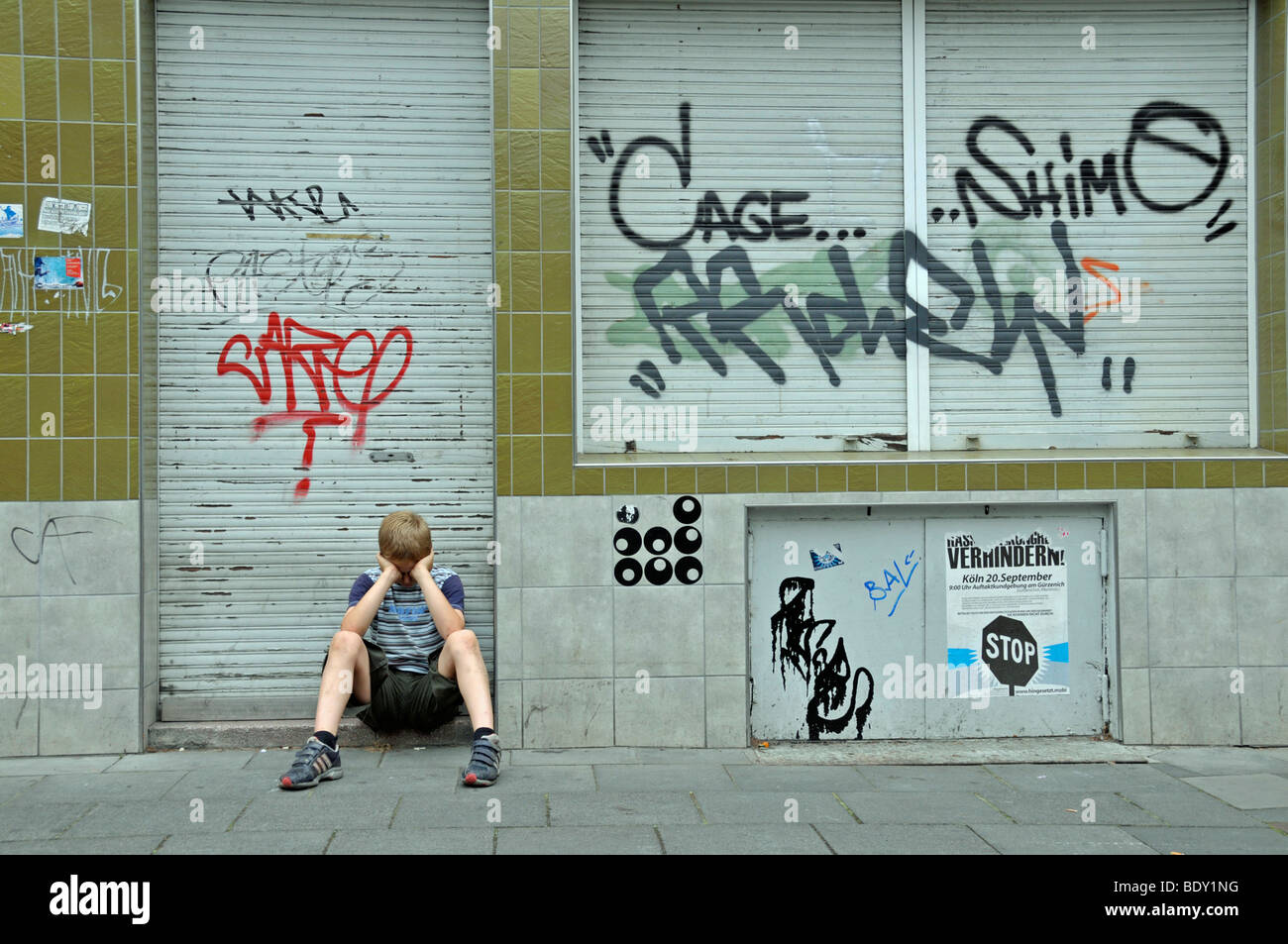 Lonely nine-year-old boy in front of a closed shop smeared with ...