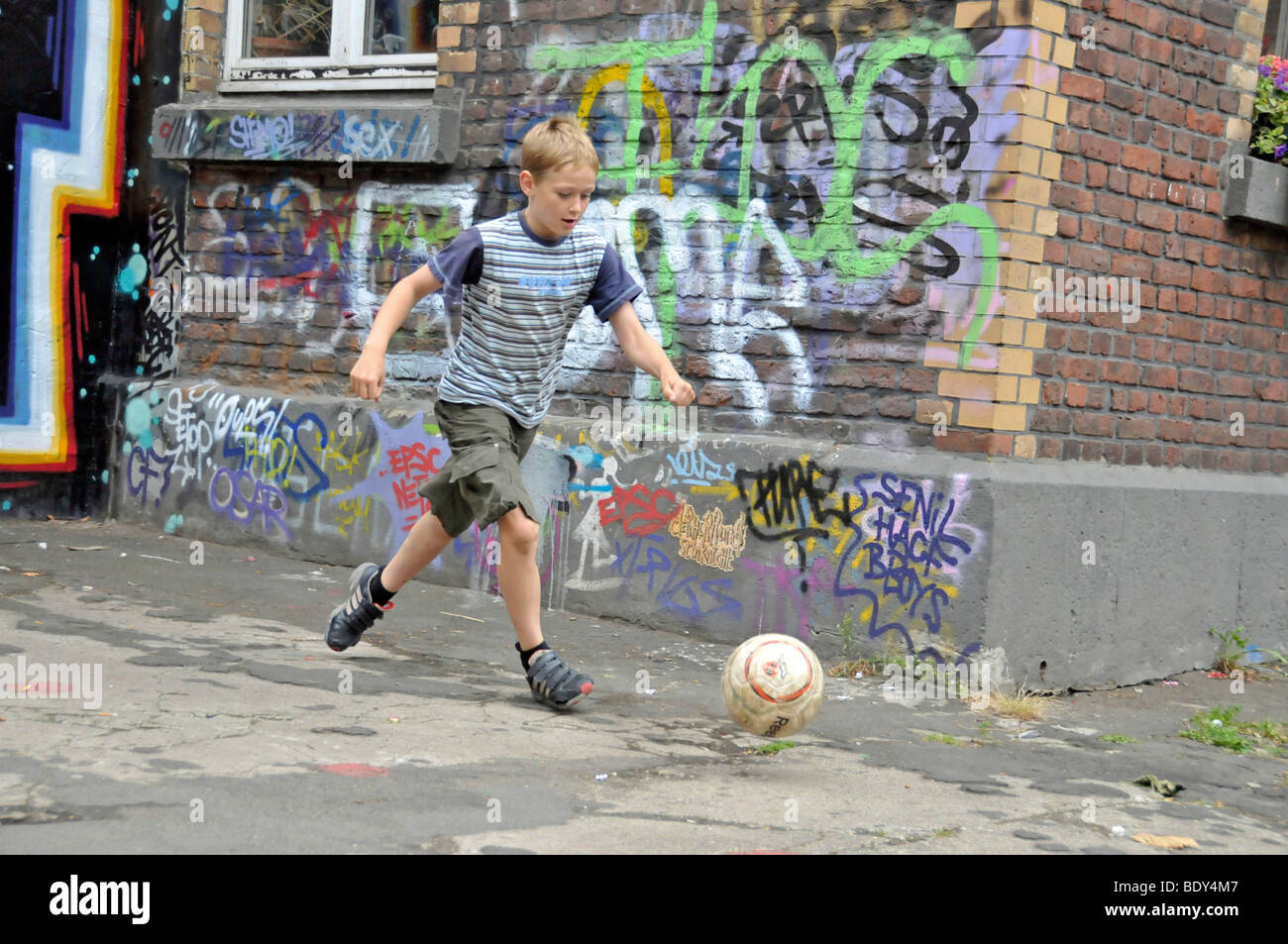 Nine-year-old boy playing with his football in front of a graffiti wall ...