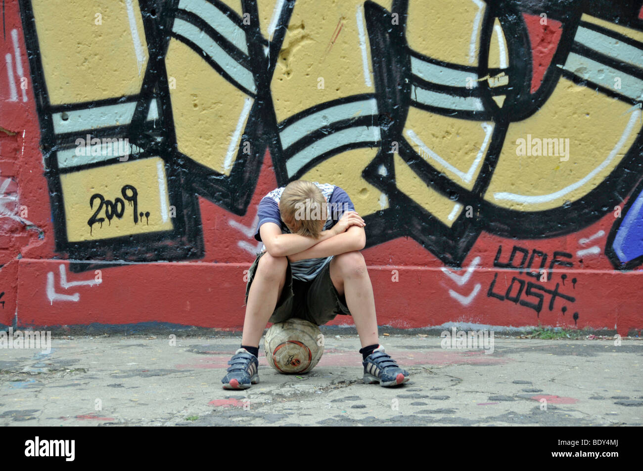 Disappointed and lonely boy with his football in front of a graffiti ...
