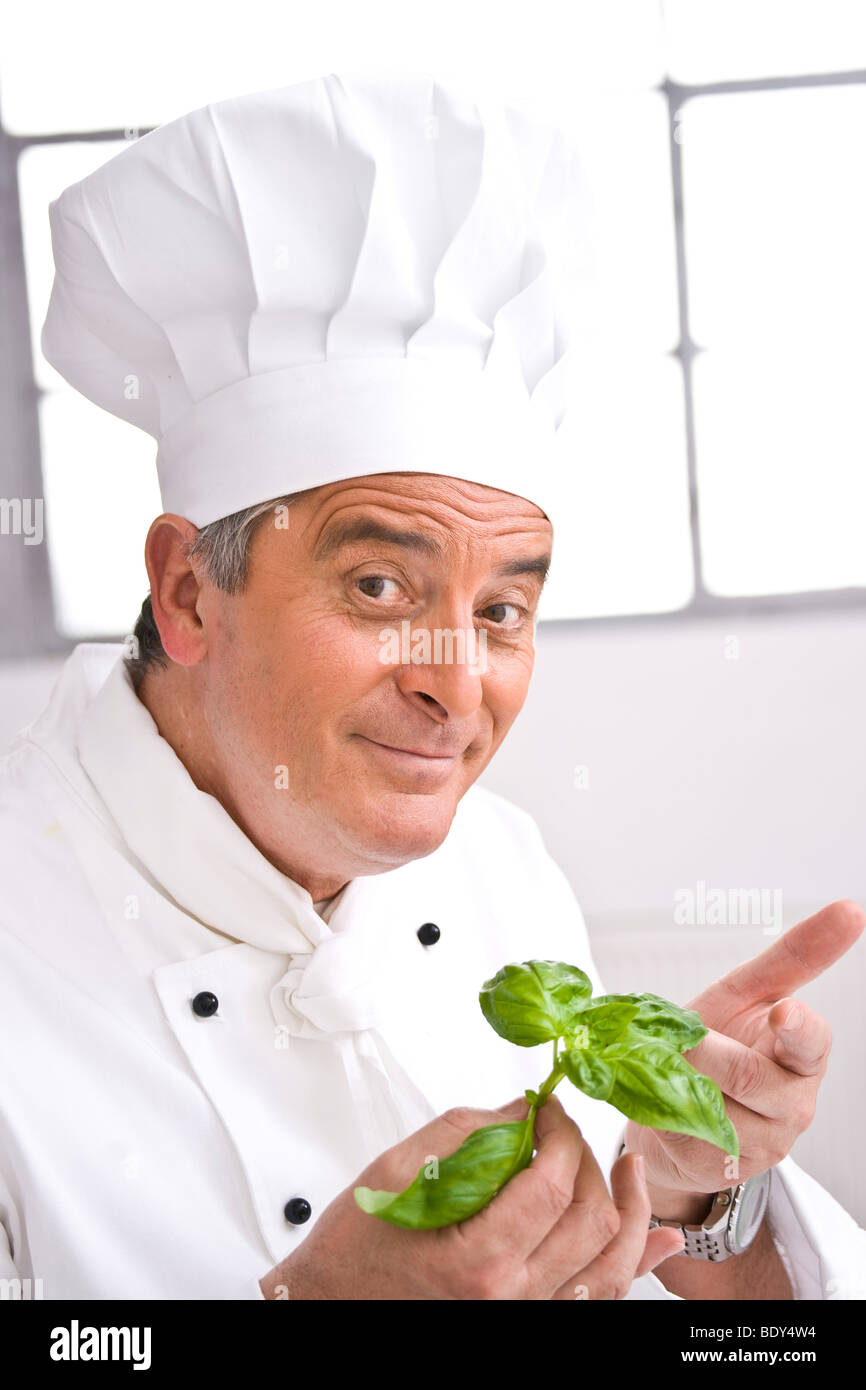 Chef wearing a chef's hat holding a sprig of basil in his hand Stock ...