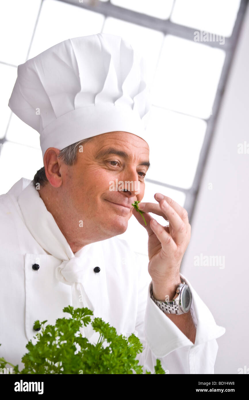 Chef wearing a chef's hat smelling parsley Stock Photo - Alamy