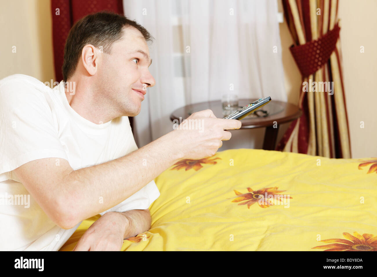 Man in bed with TV remote control Stock Photo - Alamy