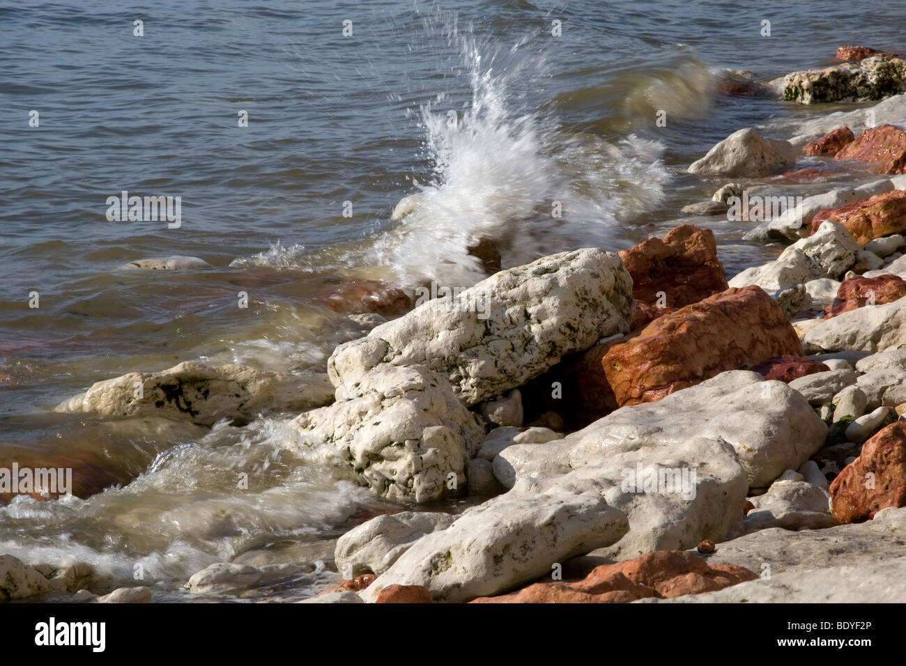 The sea lapping at the loose rocks at the base of the striped cliffs of ...