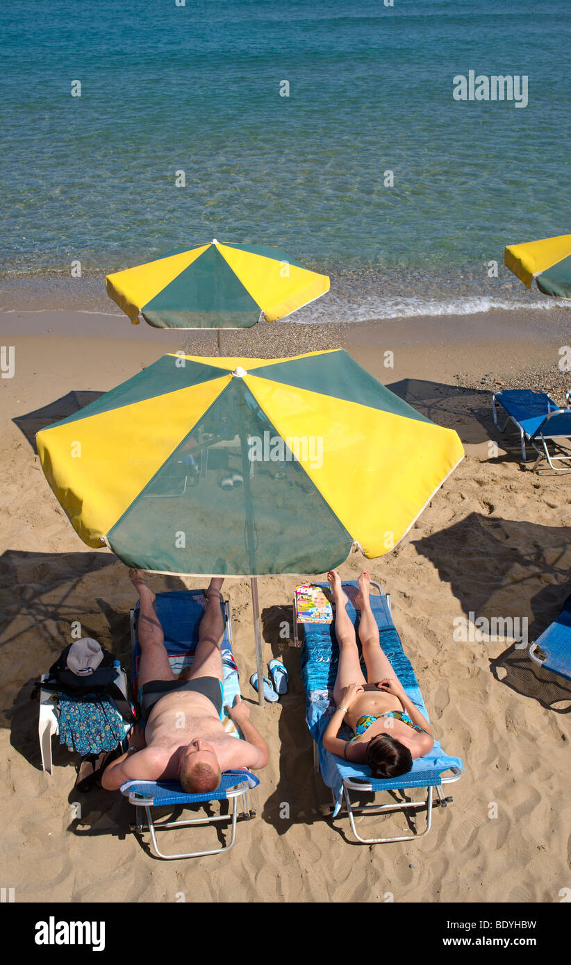 Man and woman sunbathing on beach with yellow and green umbrellas Crete ...