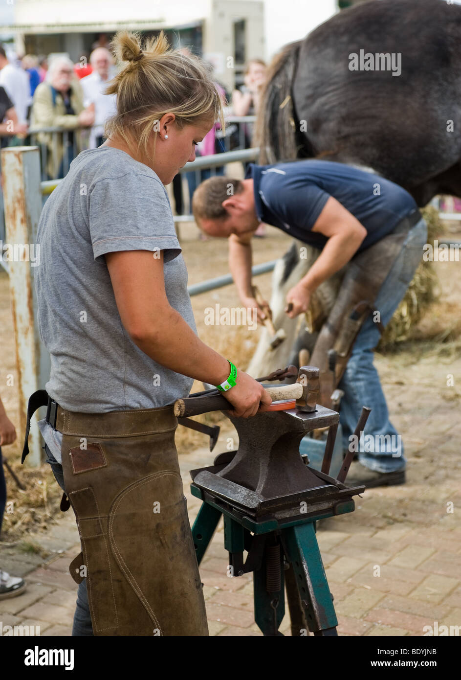 A female apprentice farrier shaping a horseshoe at a country fair in ...