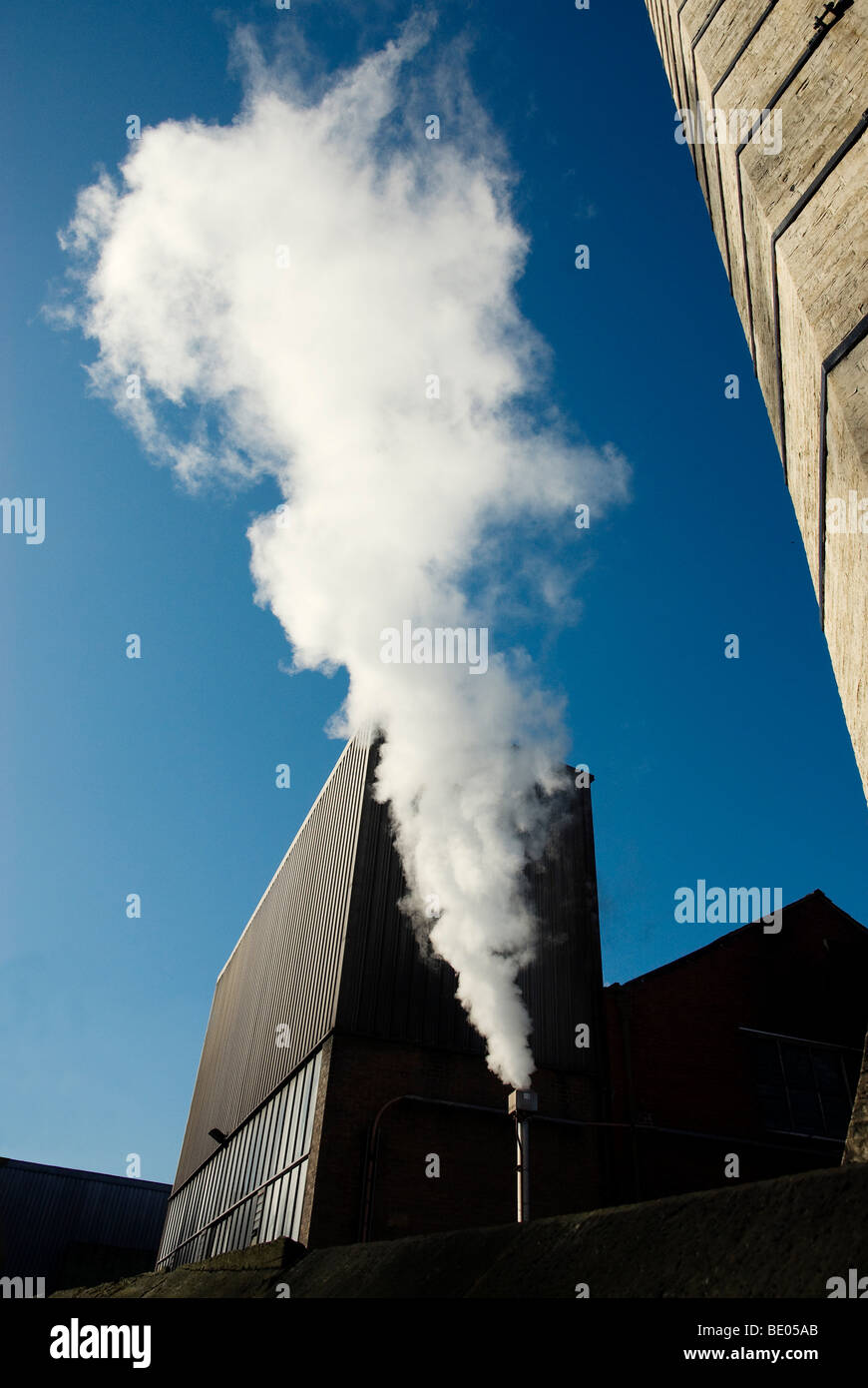 Steam coming out of pipe next to factory buildings against deep blue ...