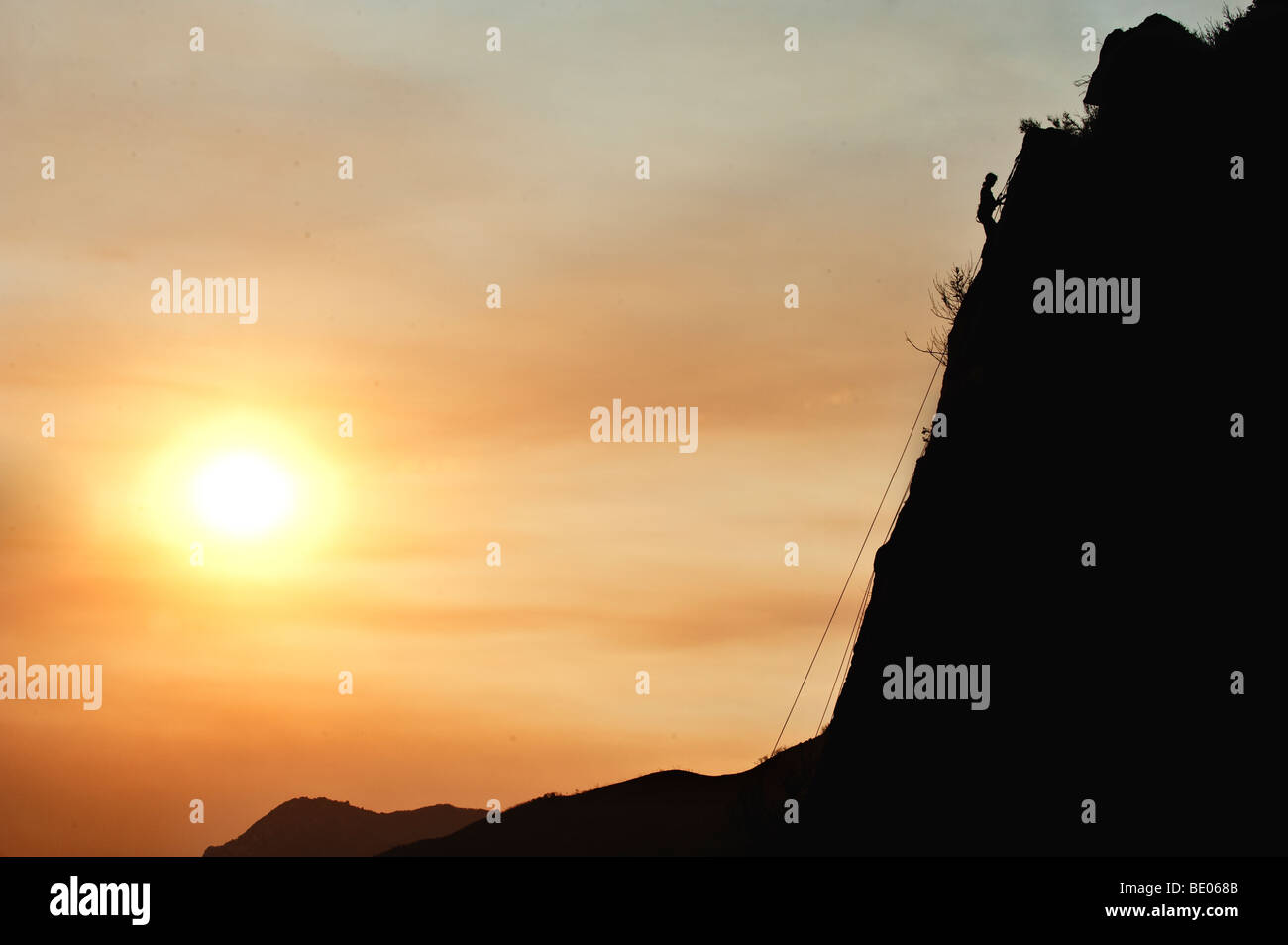A silhouetted woman climbs a rock wall during sunset in Santa Barbara ...