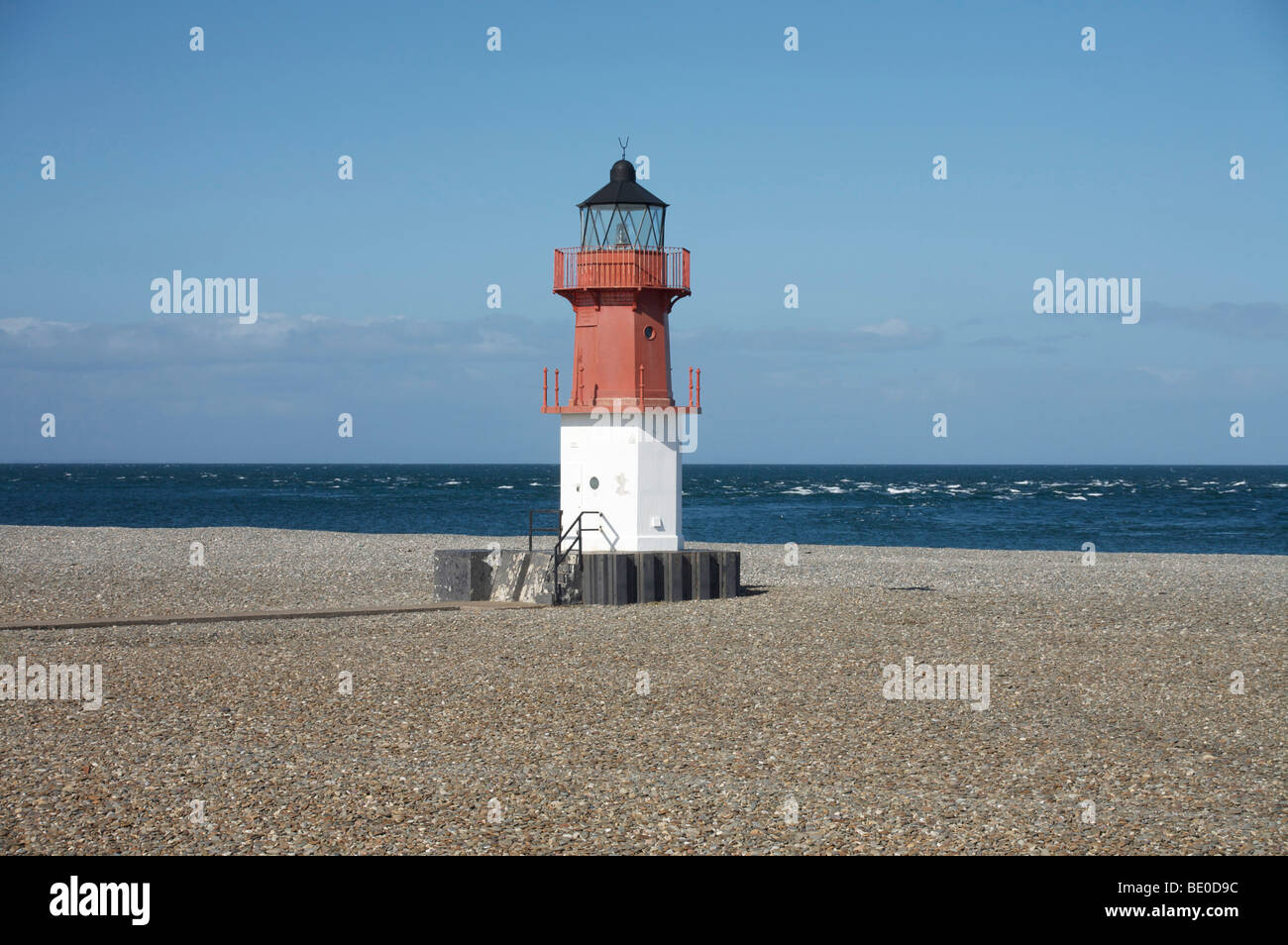 Red and white lighthouse on beautiful pebble beach with blue ocean and ...