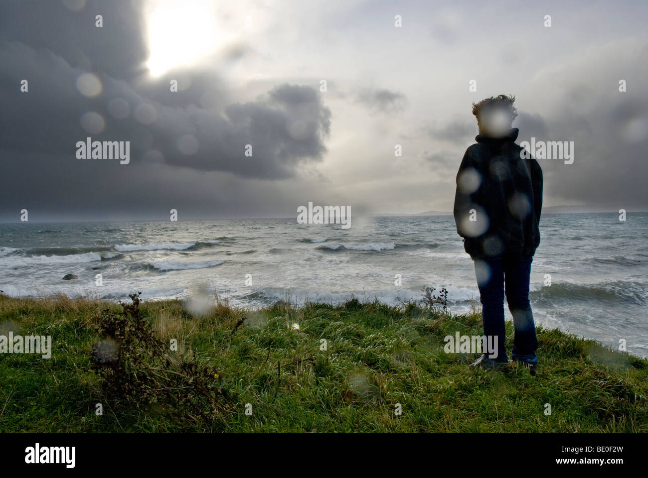 Person standing on cliff overlooking stormy sea Stock Photo - Alamy