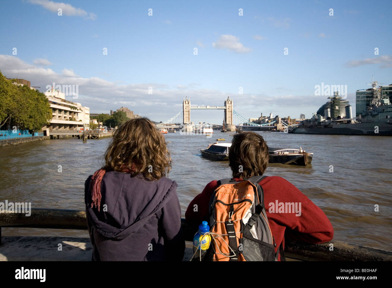 Two tourists look at Tower Bridge from the bank of the Thames in London ...
