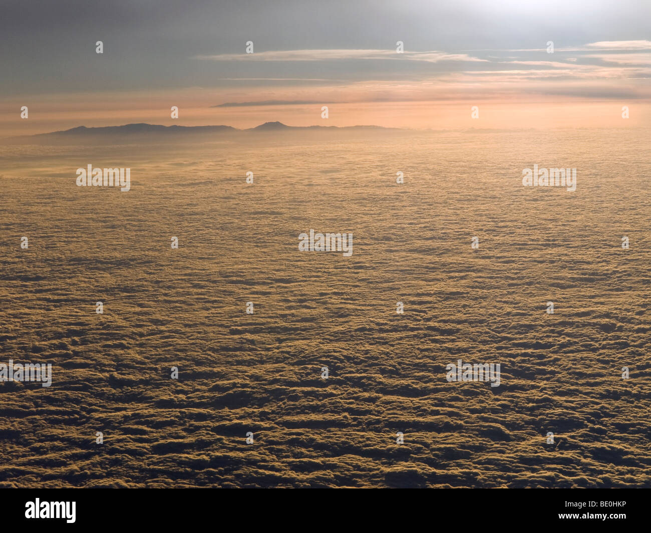 The sun declines above the clouds. A mountain is looming on the ...