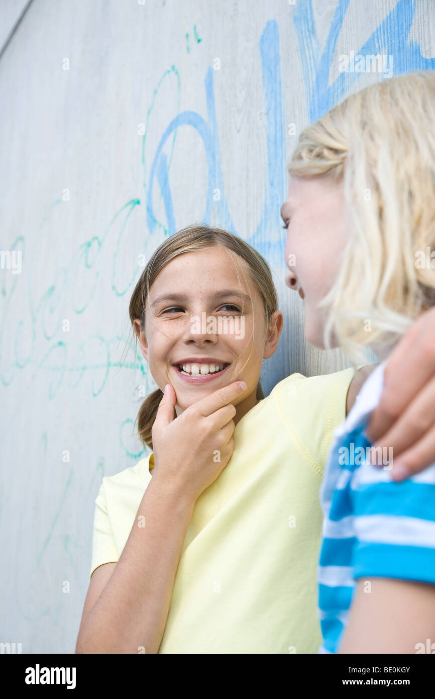 Two girls leaning against a wall, talking Stock Photo - Alamy