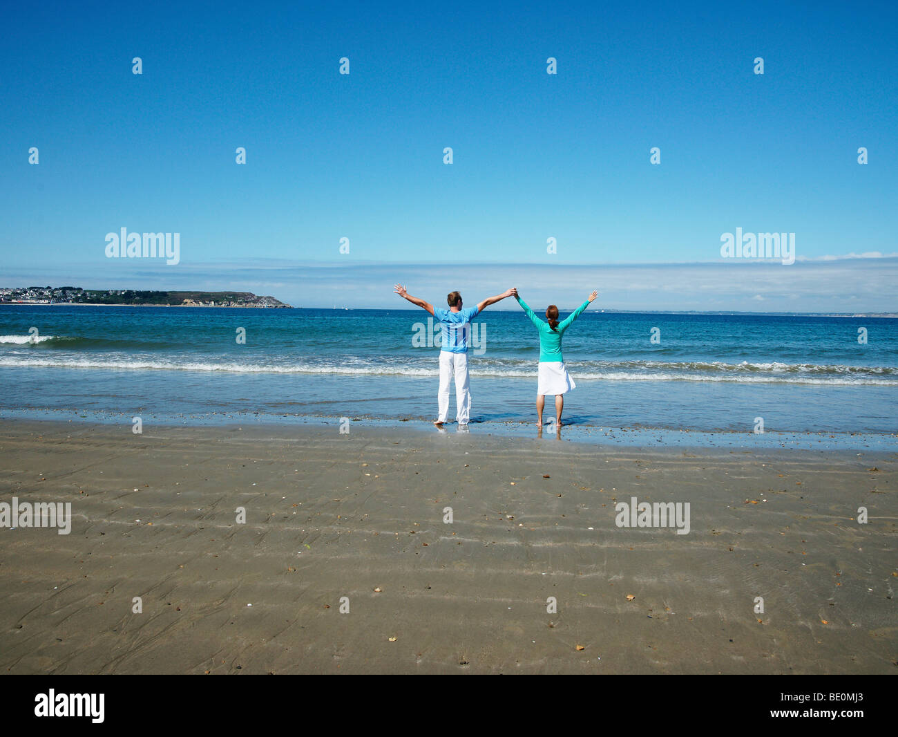 A couple standing with outstretched arms on the beach with a view on ...