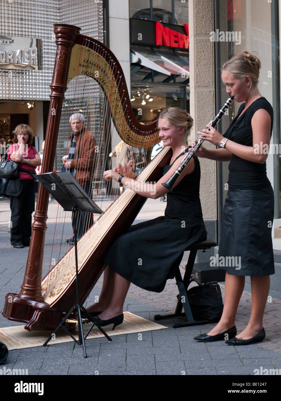 Two young female musicians playing harp and clarinet busking in ...