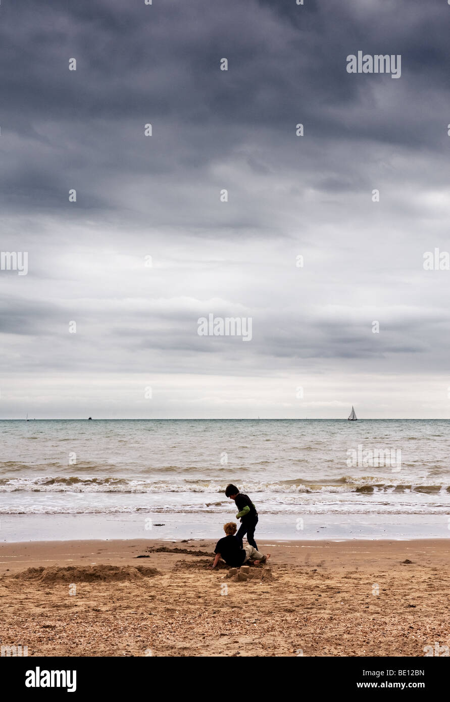 Two young boys playing on the beach on a cold day at Camber Sands in ...