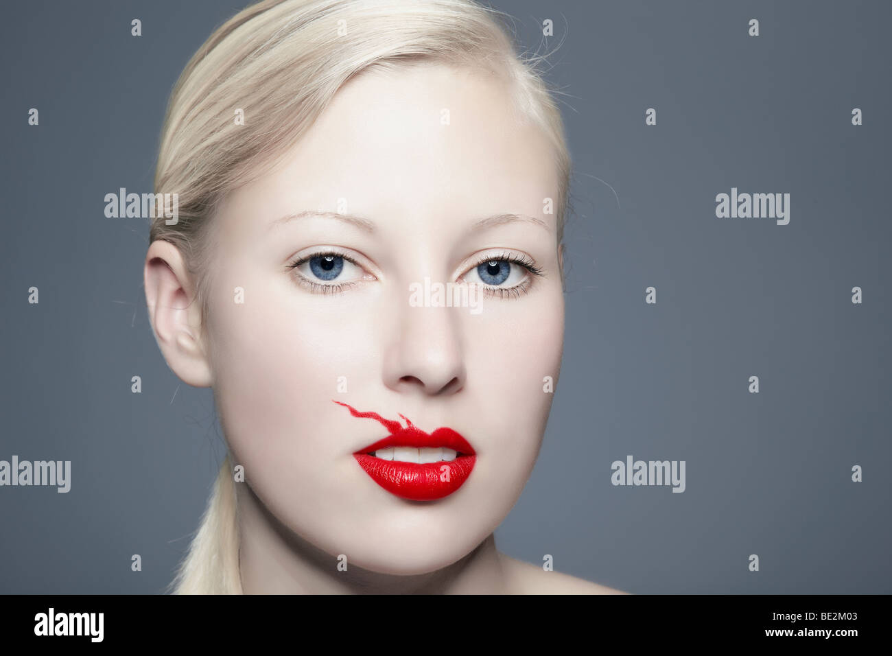 Portrait of a young blond woman with lipstick bleeding above her lip ...